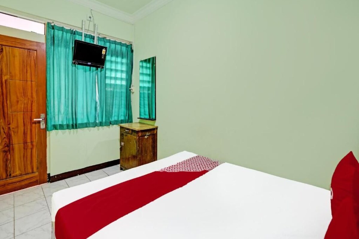 Quarto com uma cama, porta de madeira, televisão fixada na parede e um espelho.