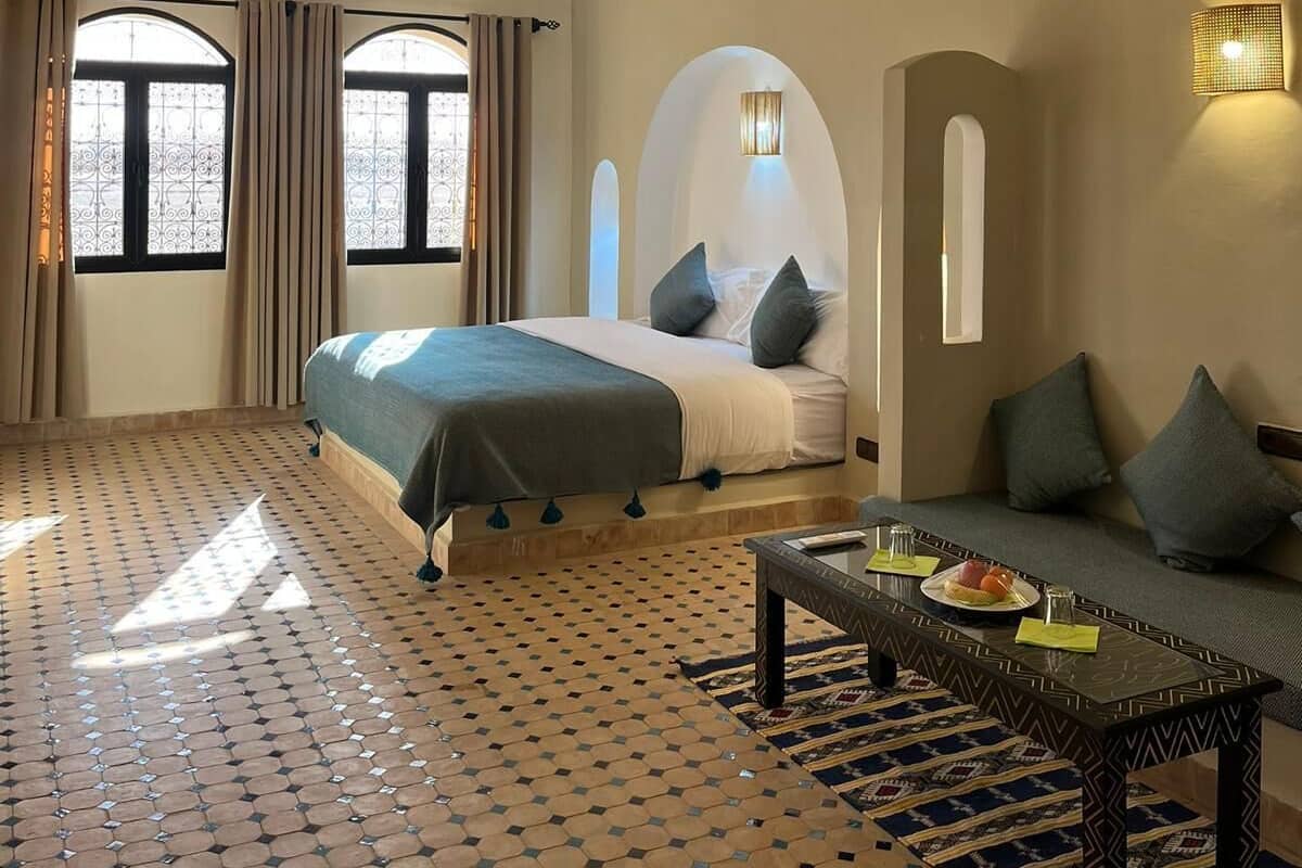 Quarto de hotel com cama, sofá, mesa de centro e piso estampado.