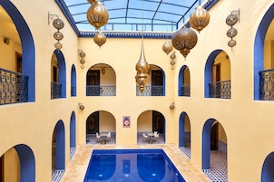 Um átrio de vários níveis com piscina central, pisos azulejados em azul e luminárias pendentes ornamentadas.