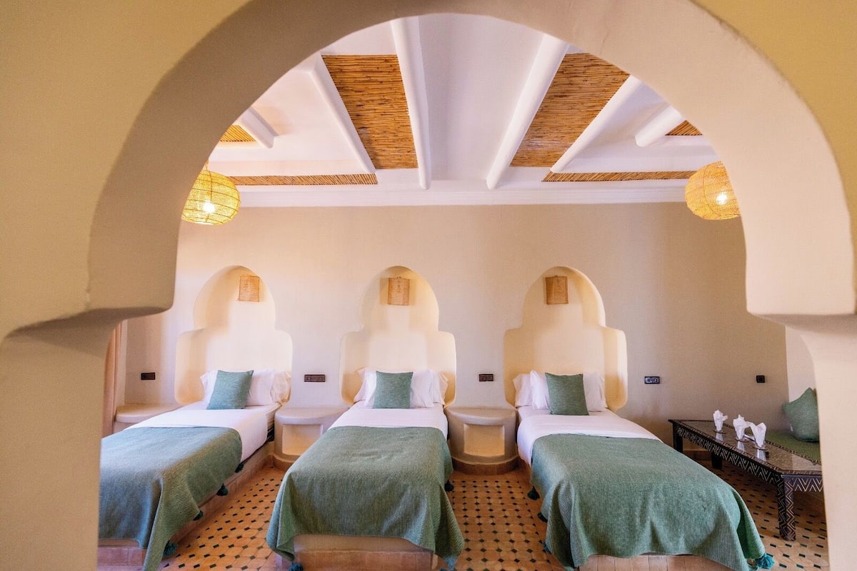 Um espaço de spa com quatro camas, uma mesinha e uma parede decorativa.