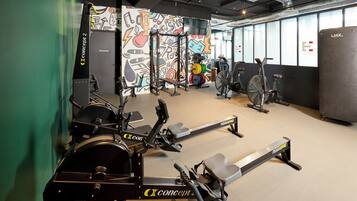 Uma academia com bicicletas ergométricas, uma máquina de remo e um banco de musculação.