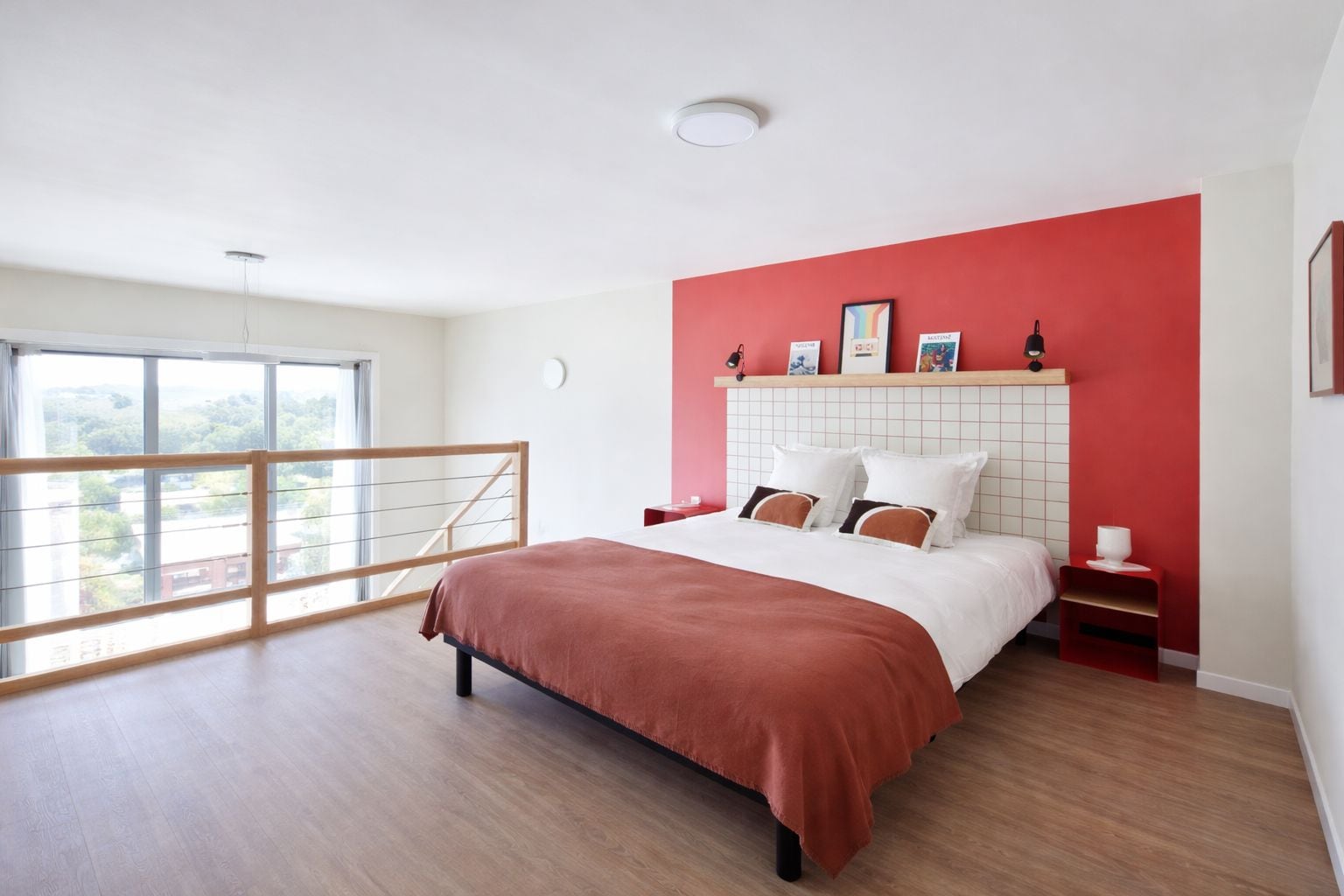 Quarto moderno com cama grande, uma parede de destaque vermelha e varanda com grade.