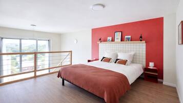 Quarto moderno com cama grande, uma parede de destaque vermelha e varanda com grade.