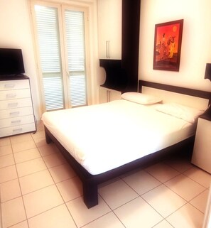 Quarto com uma cama, cômoda, televisão e um quadro na parede.