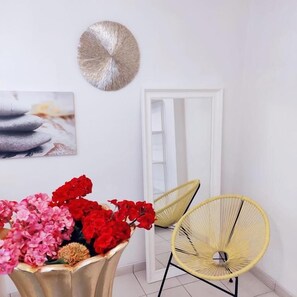 Quarto com parede branca, objeto decorativo redondo, quadro emoldurado, vaso com flores e uma cadeira amarela.