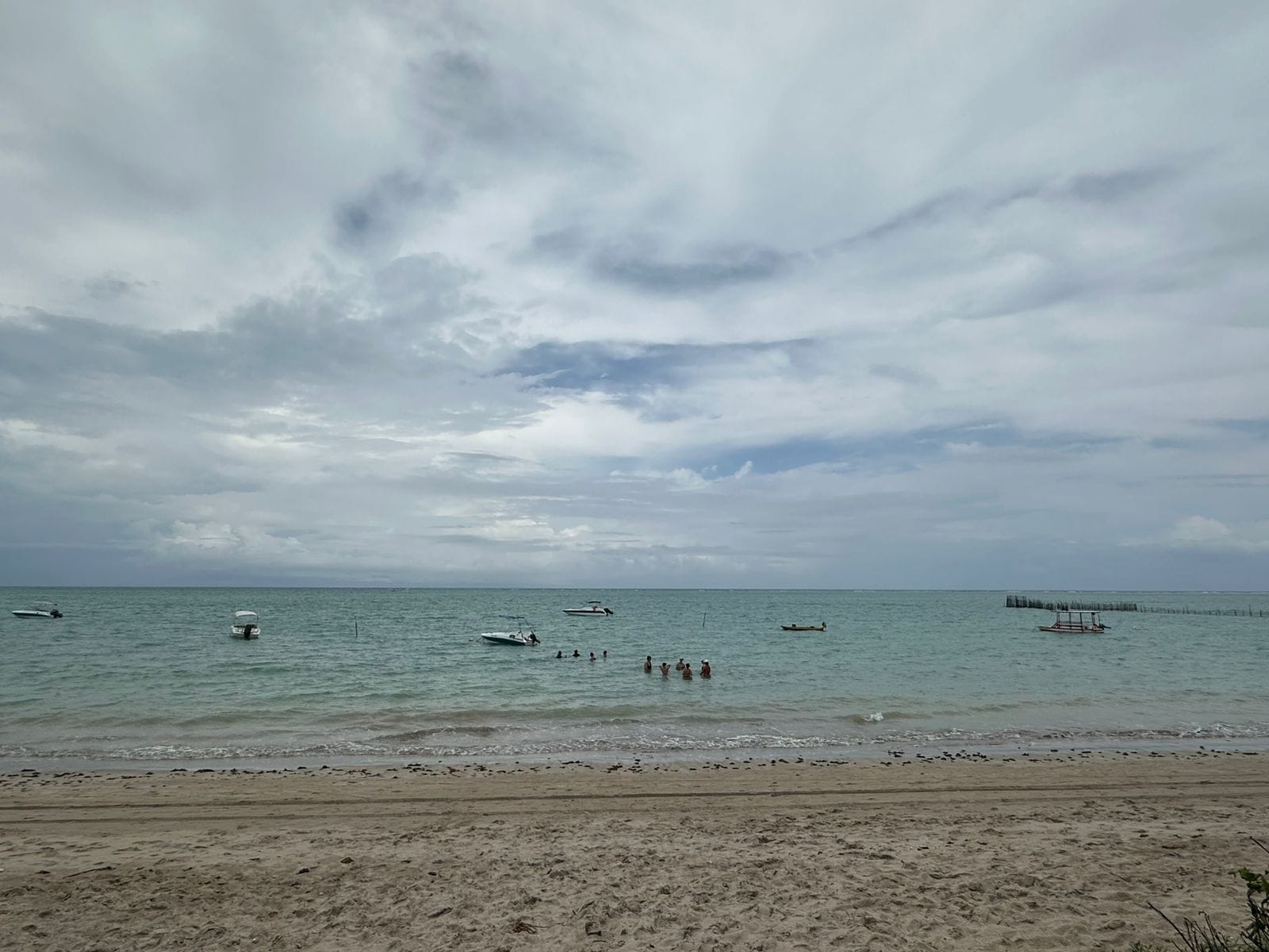 Uma praia com águas calmas, barcos e um cais.