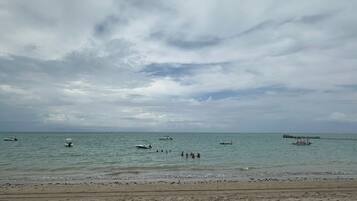 Uma praia com águas calmas, barcos e um cais.