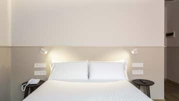 Cama bem arrumada com roupa de cama branca, mesa de cabeceira com telefone e uma pequena mesa redonda com controle remoto.