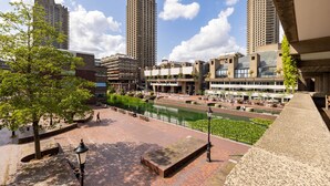Um passeio ribeirinho com bancos, uma ponte e edifícios modernos ao fundo.