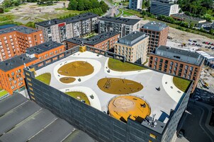 Vista aérea de um complexo moderno de edifícios com vários andares, um pátio central com áreas de estar circulares e vegetação ao redor.