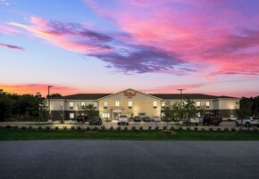Um hotel com telhado plano, entrada central e estacionamento com vários carros.