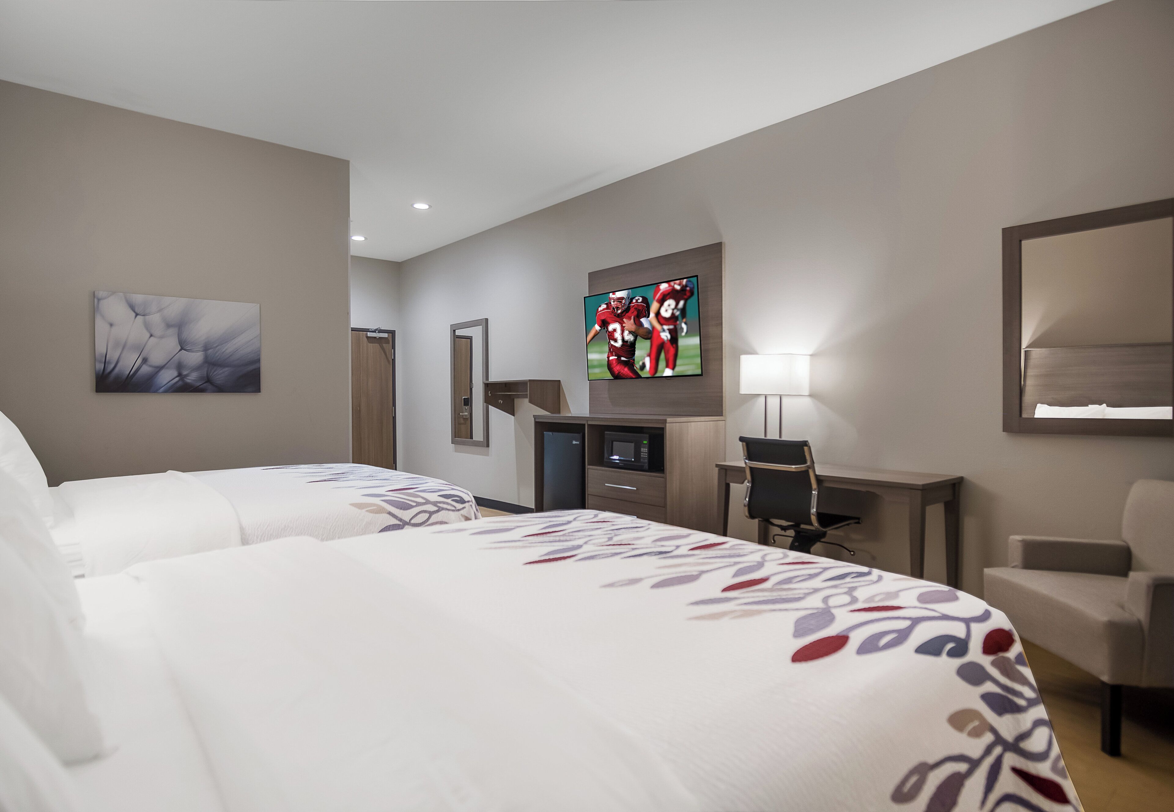 Quarto de hotel com duas camas, uma escrivaninha, uma TV e um espelho.