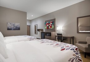 Quarto de hotel com duas camas, uma escrivaninha, uma TV e um espelho.