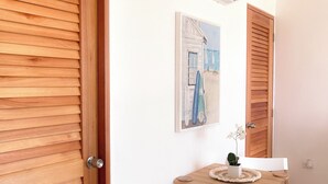 Quarto com porta de madeira, parede branca, pintura, mesa com cadeiras e ar condicionado.