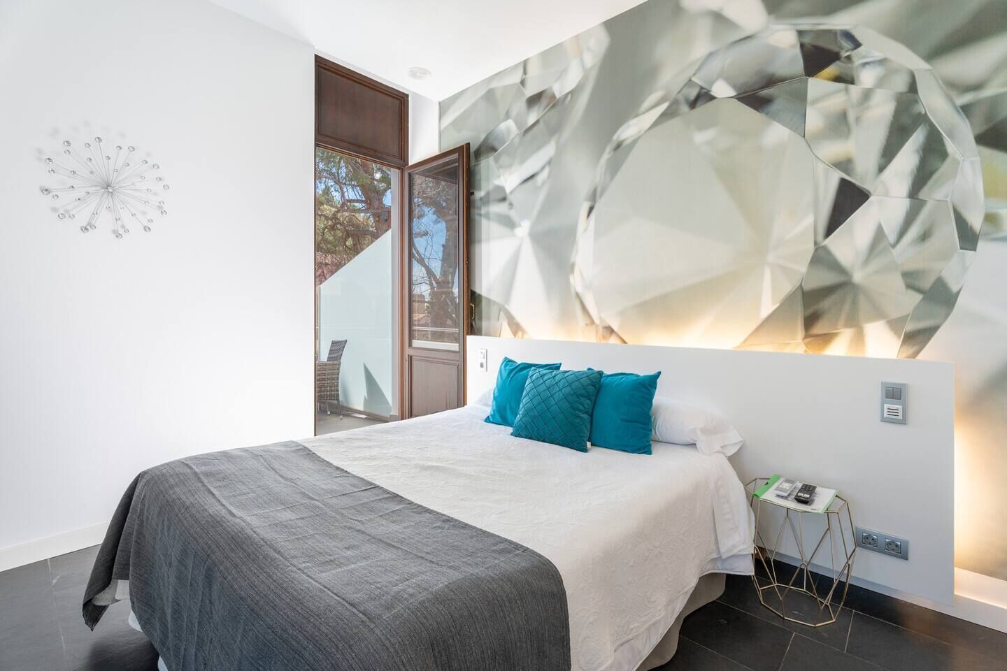 Quarto moderno com uma cama grande, uma obra de arte geométrica na parede e vista para o exterior através de uma porta de correr.