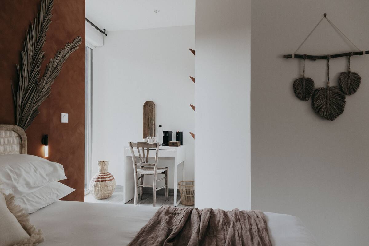 Quarto com cama, escrivaninha e cadeira. Há um vaso na escrivaninha e um objeto decorativo na parede acima dela.