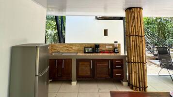Cozinha compacta com geladeira, armários de madeira, painel de backsplash de pedra e um pilar de bambu.