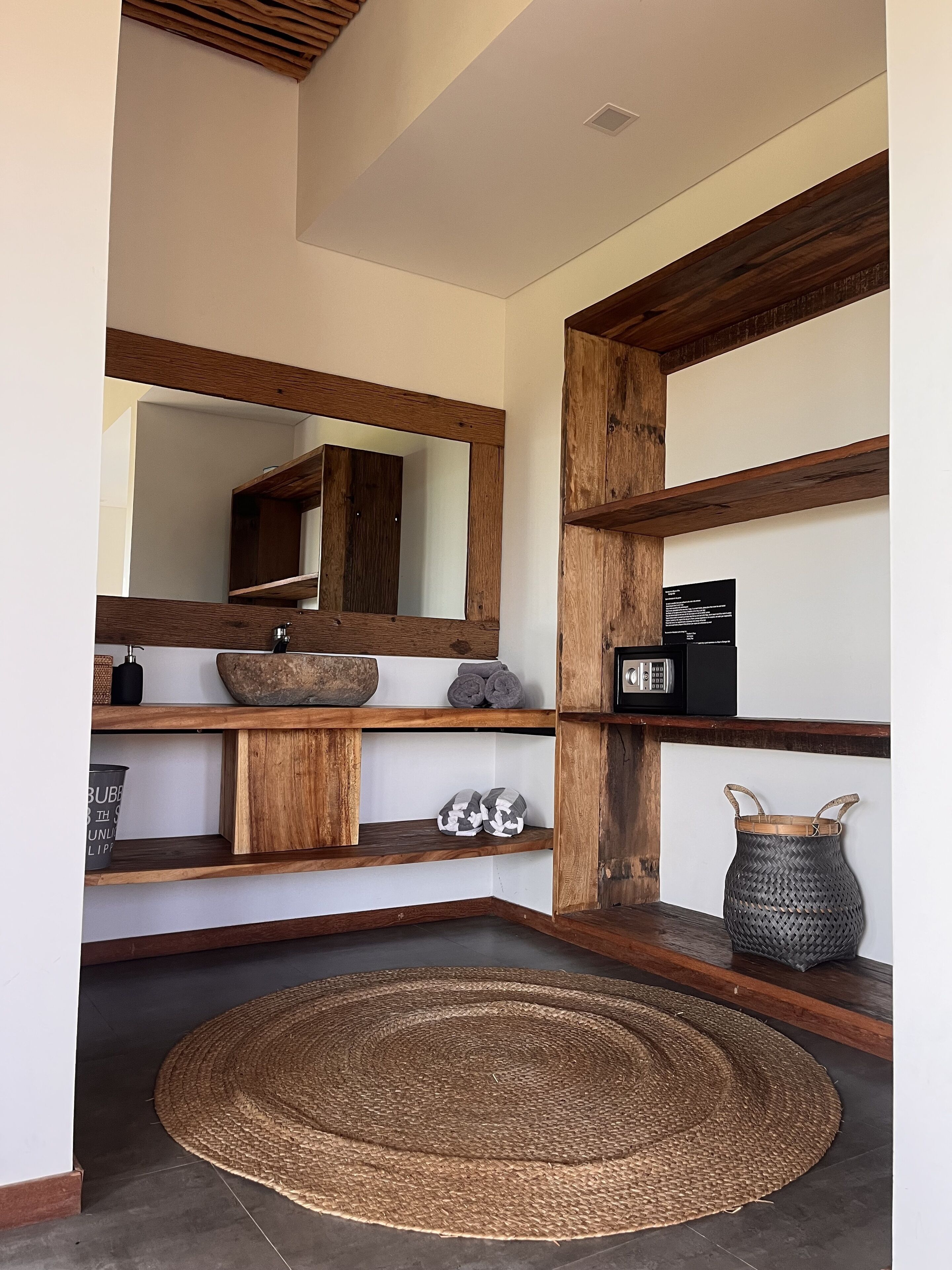 Um interior moderno com vigas de madeira, um espelho grande, prateleiras com diversos objetos e um tapete tecido.