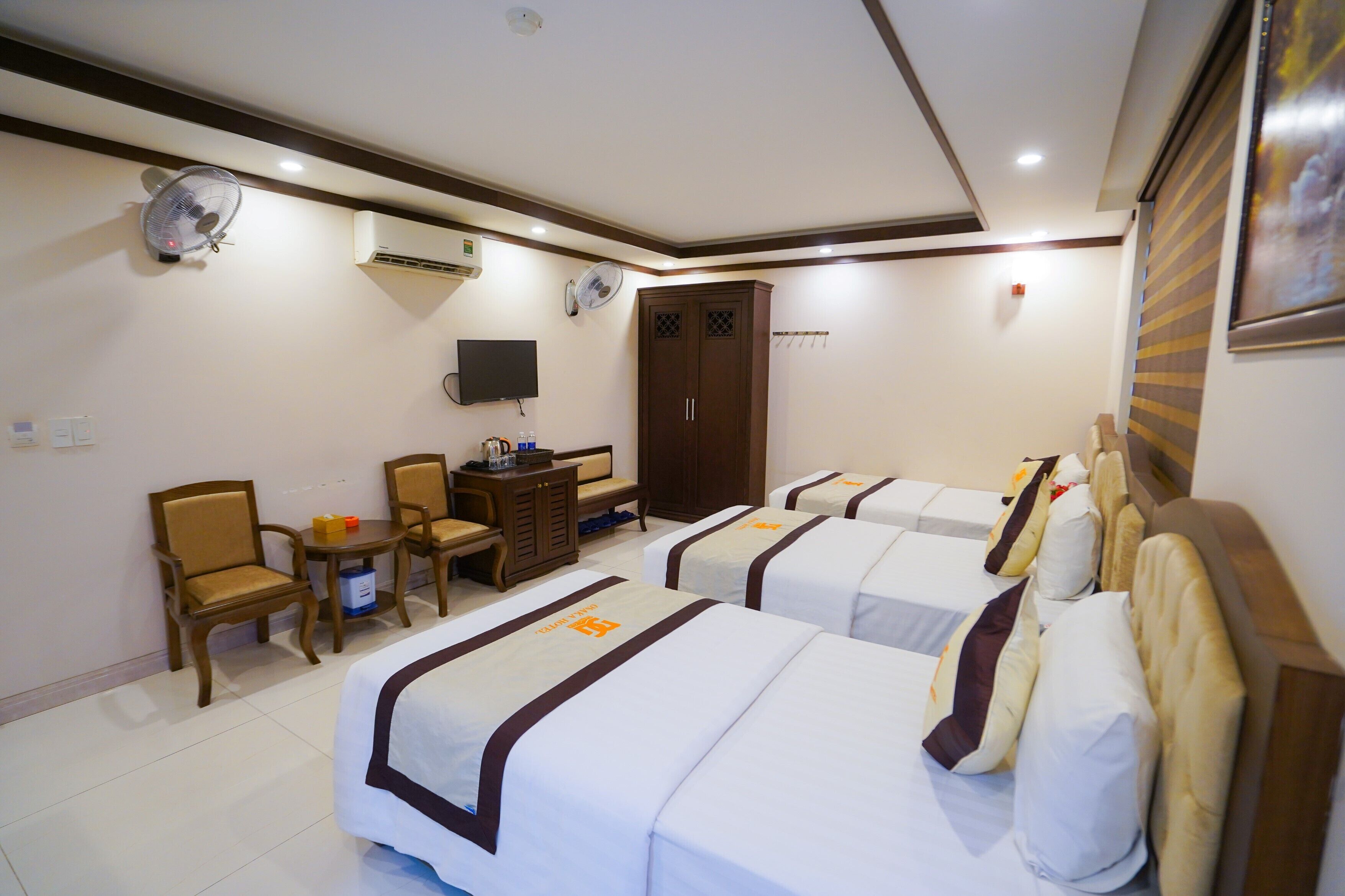 Quarto de hotel com quatro camas, uma escrivaninha com cadeira, televisão e guarda-roupa.