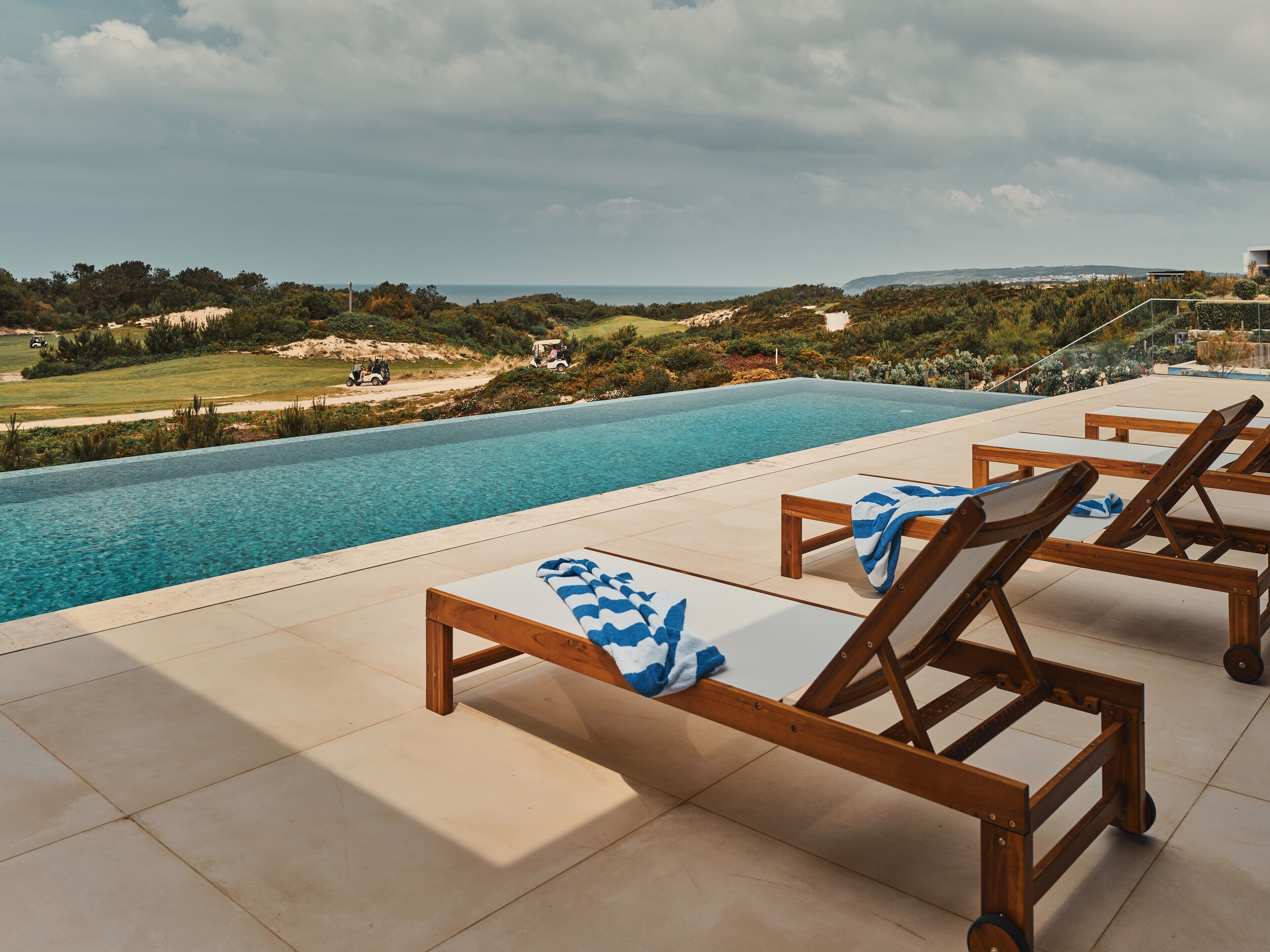 Área de piscina com espreguiçadeiras e vista para um campo de golfe.