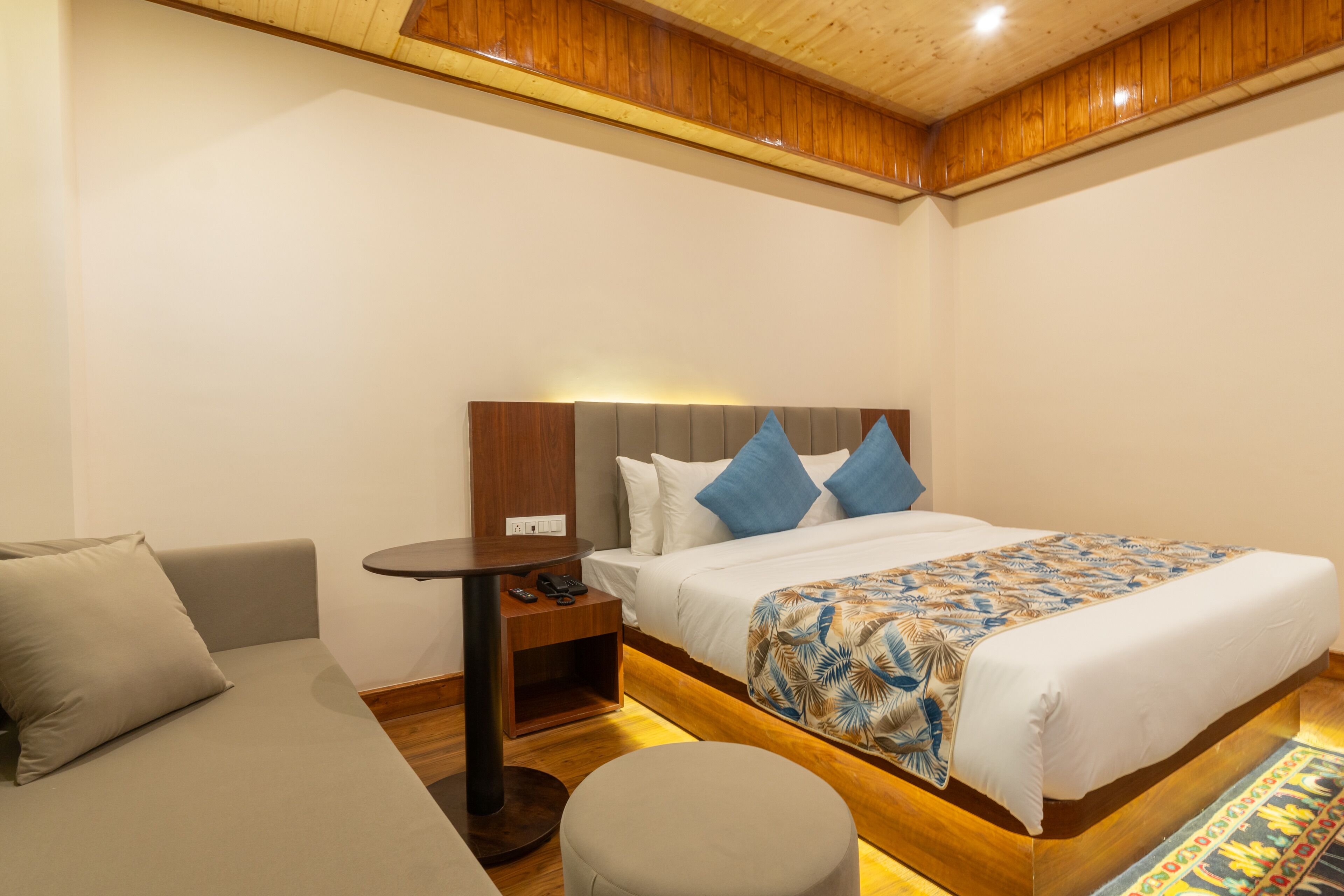 Quarto de hotel com cama, sofá, pequena mesa e teto de madeira.