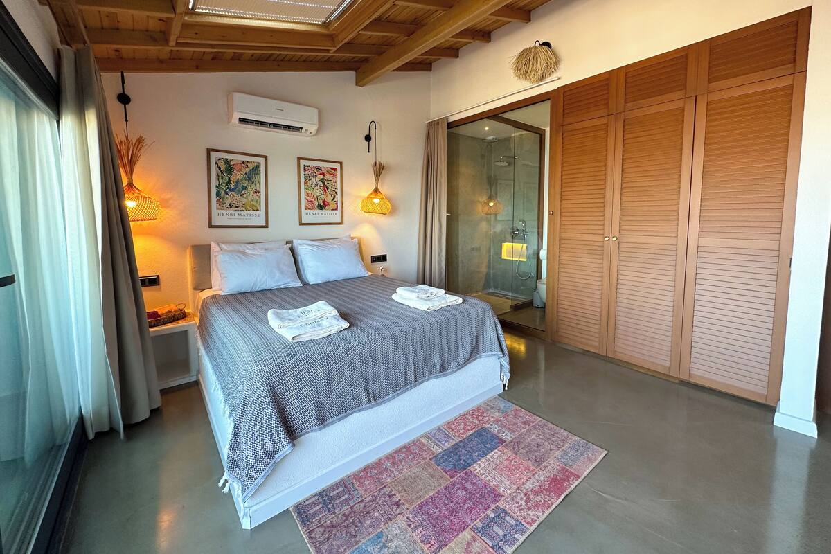 Quarto com cama, chuveiro de vidro, guarda-roupa de madeira e duas obras de arte na parede.