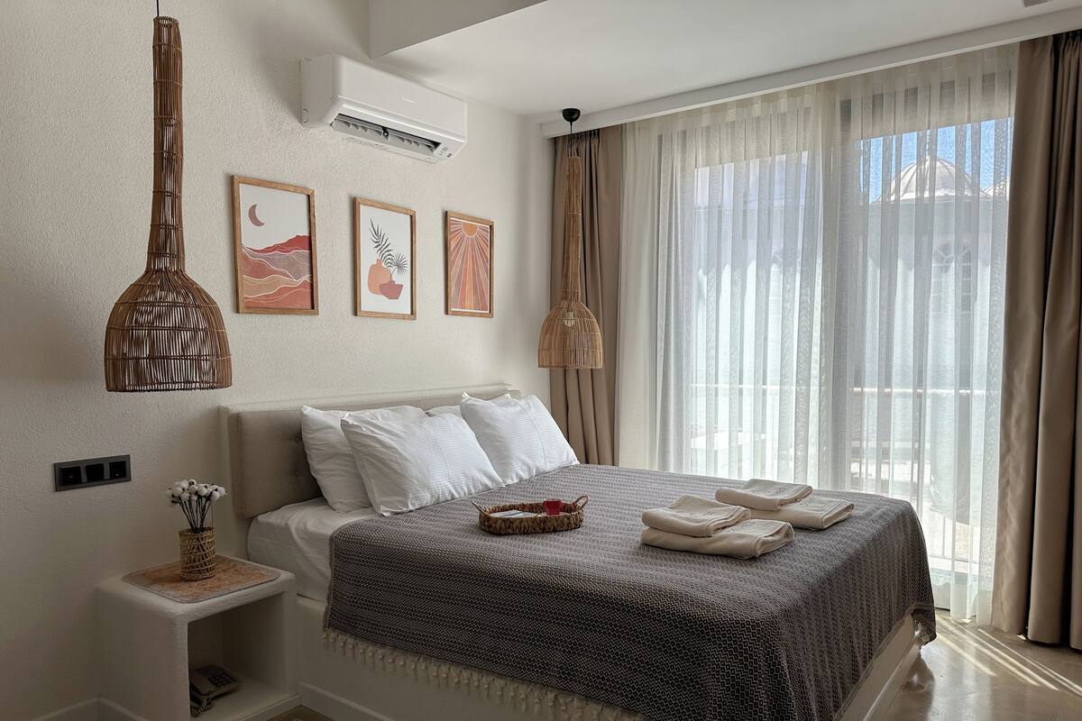 Quarto bem arrumado com cama, mesas de cabeceira, ar-condicionado fixado na parede e quadros decorativos.