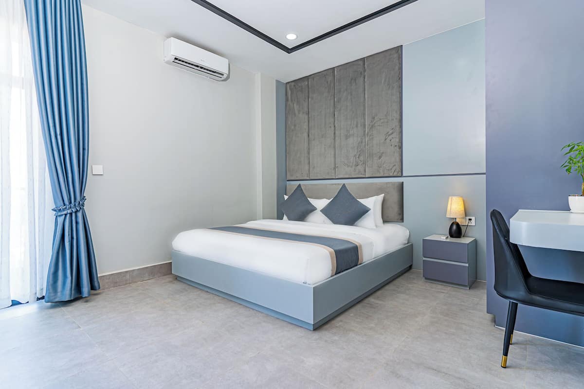 Quarto moderno com cama, mesas de cabeceira, escrivaninha e uma cadeira.