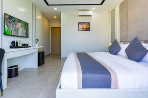 Quarto de hotel moderno com uma cama grande, uma escrivaninha com televisão e uma pequena planta.
