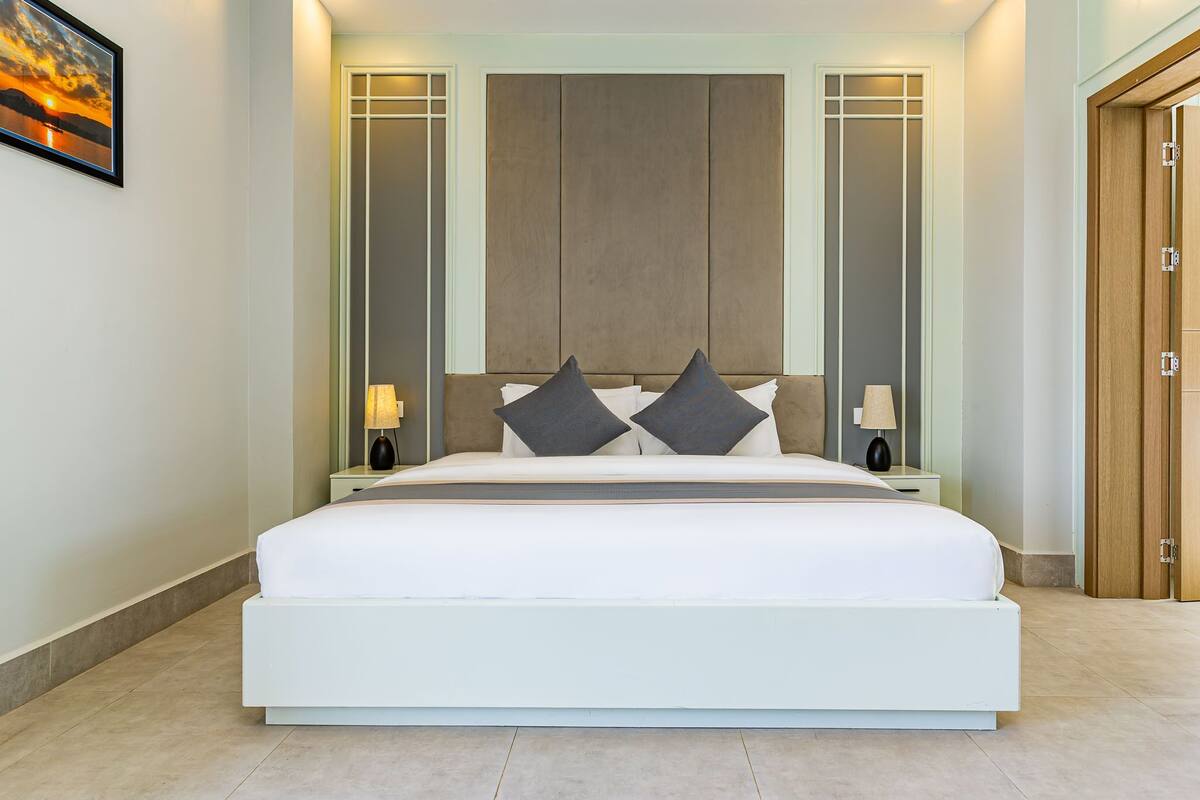 Quarto moderno com cama grande, duas mesas de cabeceira com luminárias e porta de madeira.