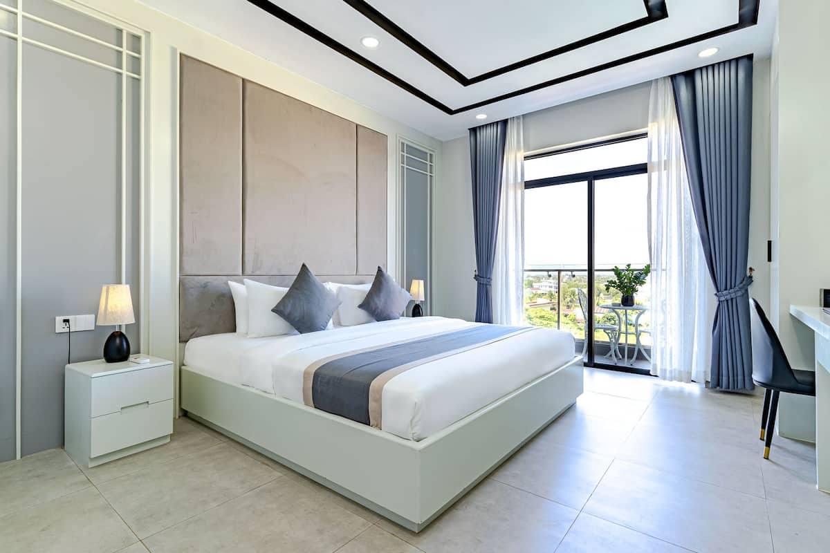 Quarto moderno com uma cama grande, mesas de cabeceira, uma escrivaninha e uma varanda com vista.