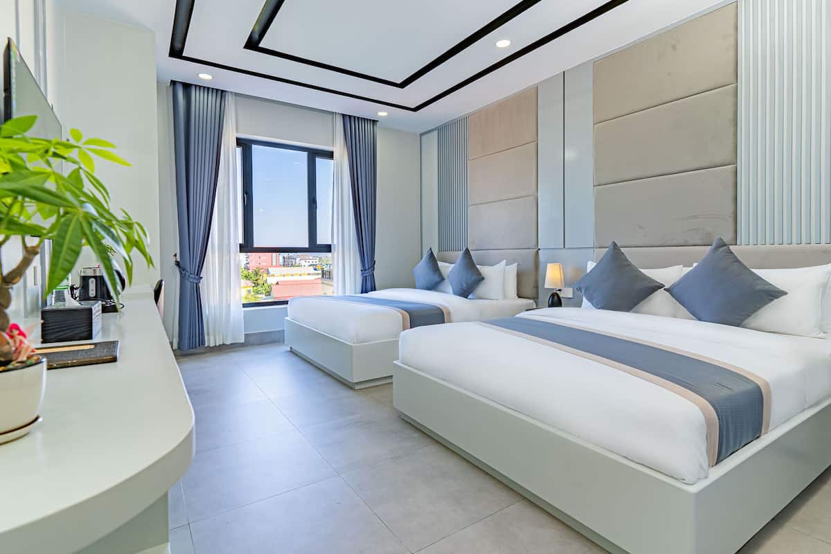 Quarto de hotel moderno com duas camas, uma escrivaninha curva e uma janela grande com cortinas.
