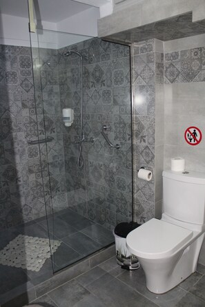 Um banheiro com chuveiro em box de vidro, vaso sanitário e bidê.