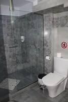 Um banheiro com chuveiro em box de vidro, vaso sanitário e bidê.
