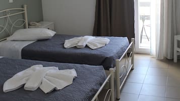 Quarto de hotel com duas camas, uma mesa de cabeceira, uma luminária e uma janela com cortinas.