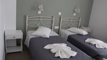 Quarto duplo com duas camas, cada uma com cabeceira branca, mesa de cabeceira e luminária.