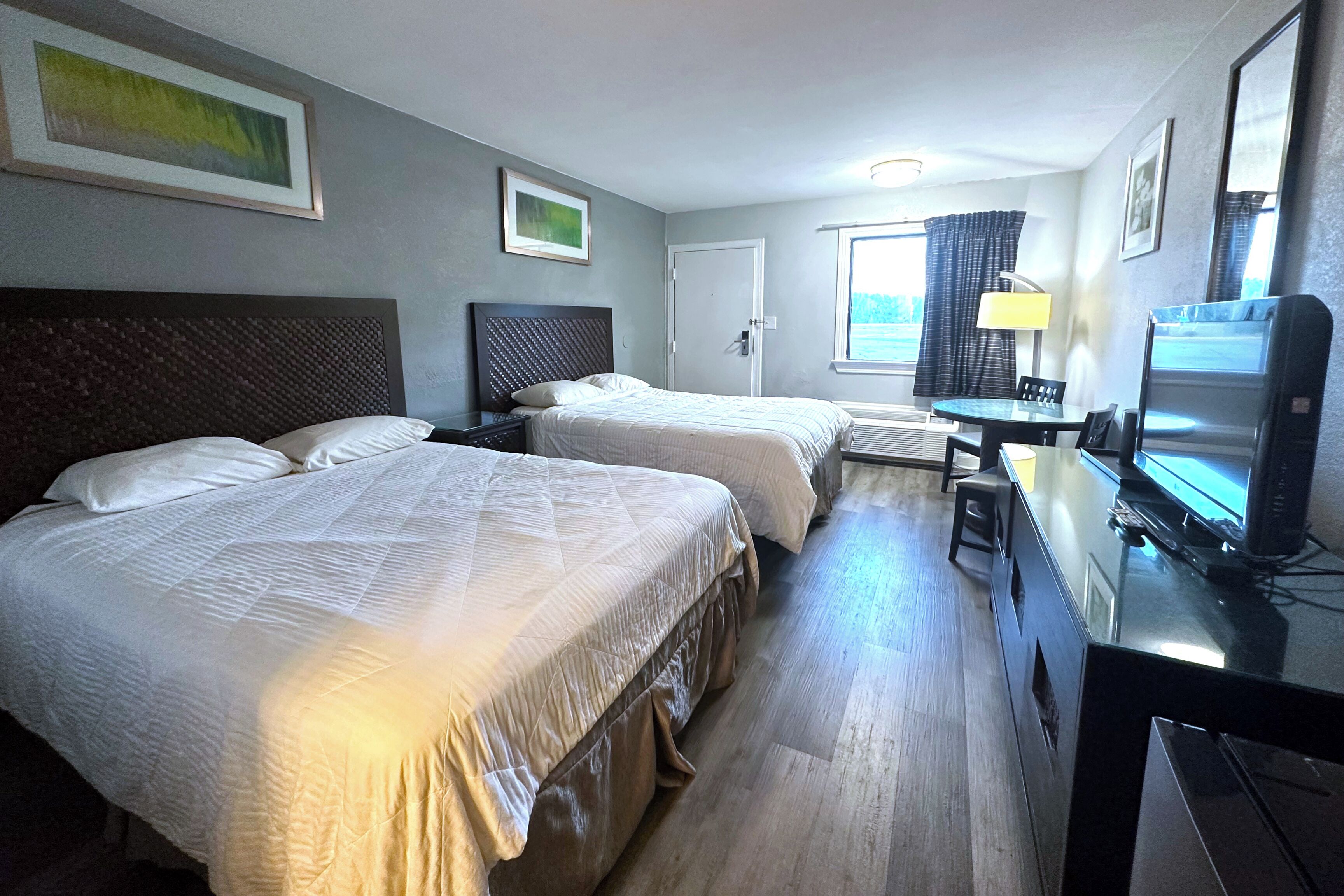 Quarto de hotel com duas camas, uma mesa de trabalho com televisão e janela com cortinas.
