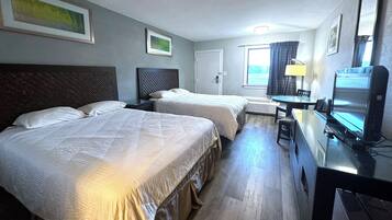 Quarto de hotel com duas camas, uma mesa de trabalho com televisão e janela com cortinas.