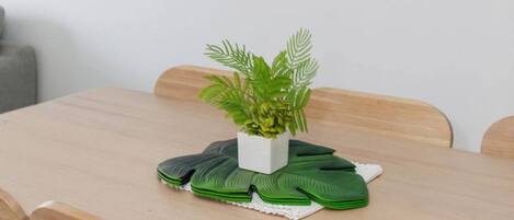 Uma área de refeições com uma mesa de madeira, cadeiras, um vaso de planta e uma pintura de um cais e oceano.