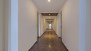 Um corredor comprido e estreito com soalho de pedra polida e paredes brancas.