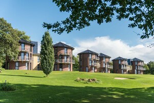 Edifícios de apartamentos de tijolo com varandas, um gramado e árvores.