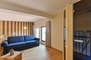 Uma sala de estar com sofá azul, piso de madeira, escada de madeira e parede listrada.