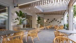 Uma área de café ao ar livre com cadeiras e mesas de madeira, plantas em vasos e um design de teto moderno.