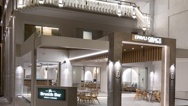 Um edifício de vários andares com um restaurante chamado "EPAVLU GRACE" no andar térreo, apresentando um design moderno com varandas e uma área de estar visível no interior.