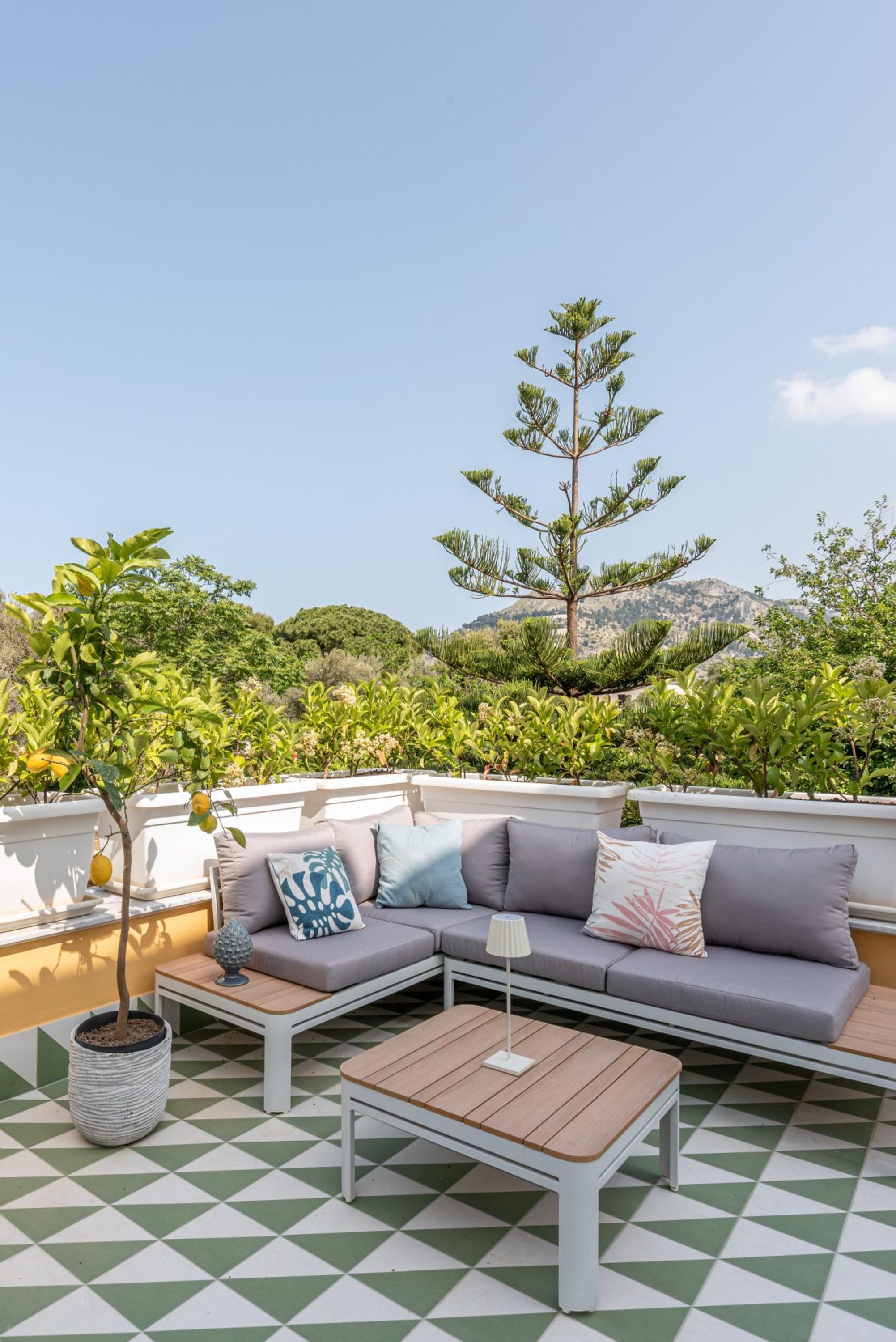 Um terraço com um sofá cinzento, uma mesa de madeira e um vaso de planta.