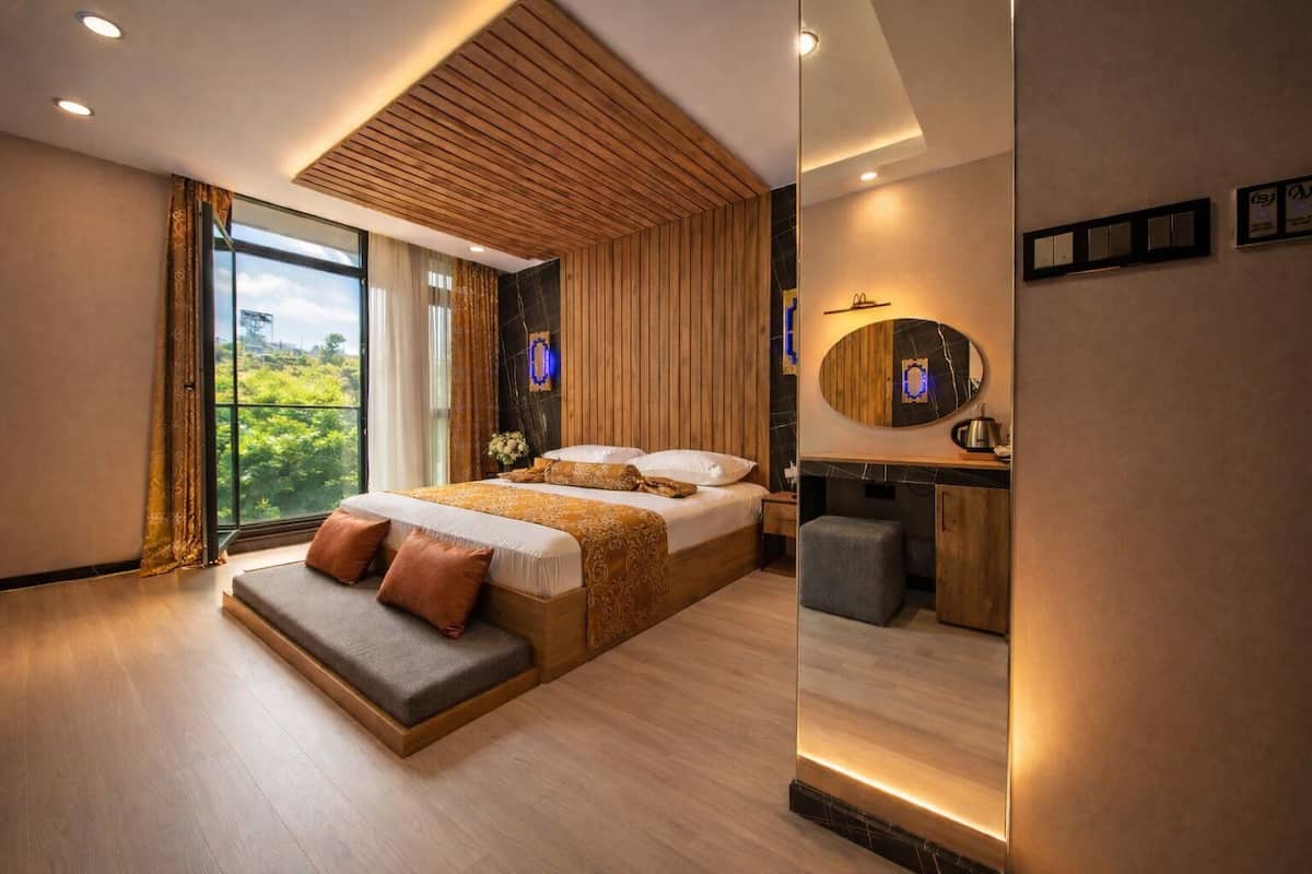 Quarto moderno com cama grande, uma escrivaninha e vista para área verde.