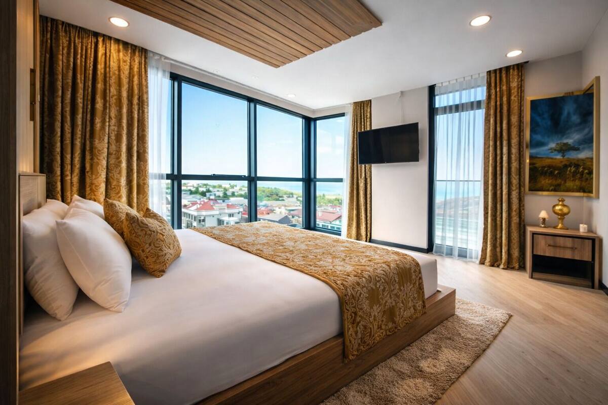 Quarto de hotel moderno com uma cama grande, televisão de tela plana, um quadro e vista para a cidade.