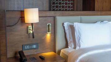 Quarto de hotel com cabeceira de madeira, mesa de cabeceira com luminária, controle remoto e tomada.