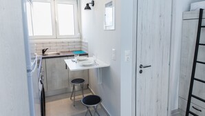 Cozinha compacta com bancada branca, pia e um banquinho.
