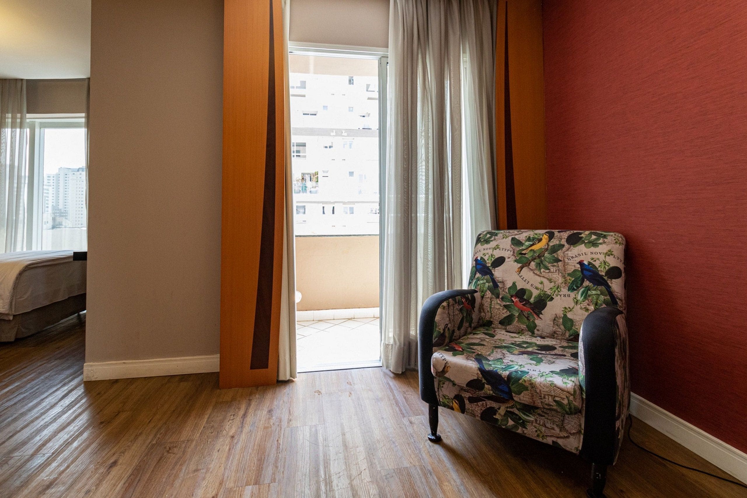 Um quarto com piso de madeira, parede vermelha e uma cadeira com estampa de pássaros.